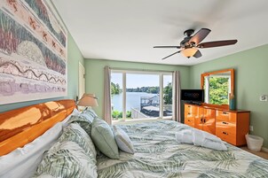 Quarto com cama, ventilador de teto, televisão e vista para um lago.
