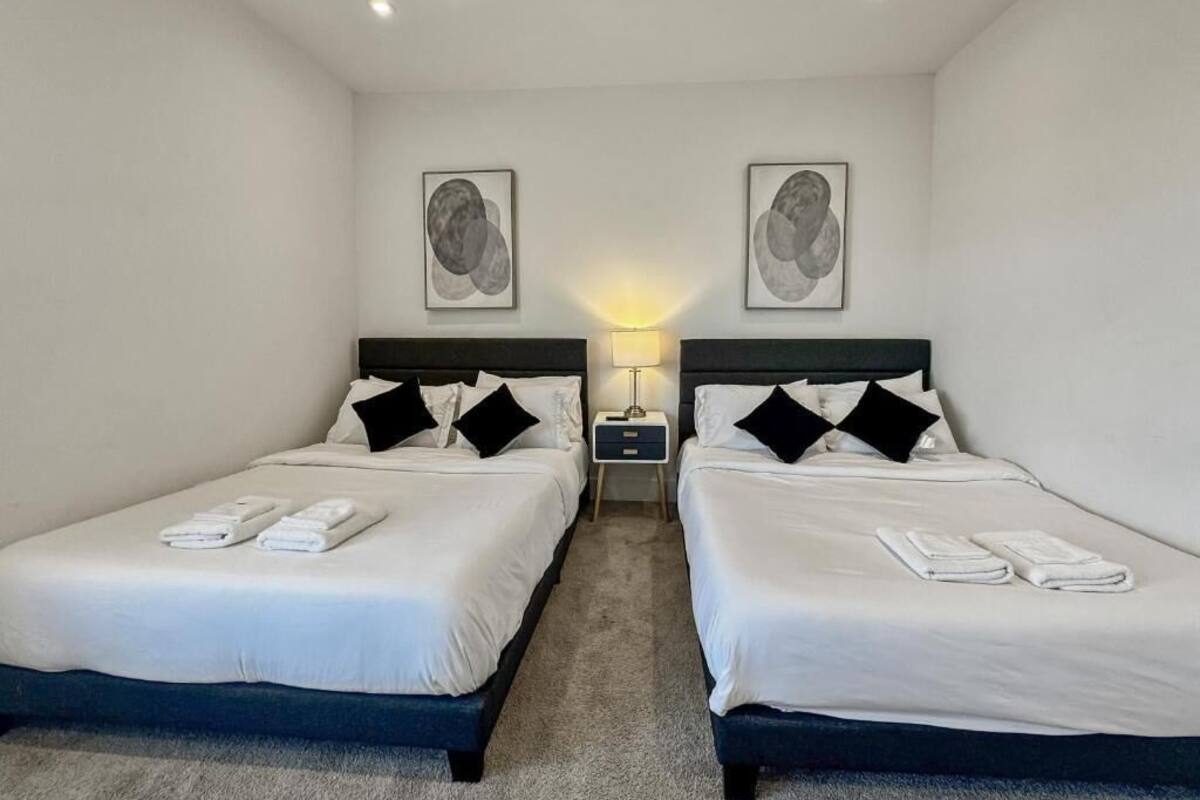 Quarto de hotel com duas camas, uma mesa de cabeceira, uma luminária e duas fotos emolduradas na parede.