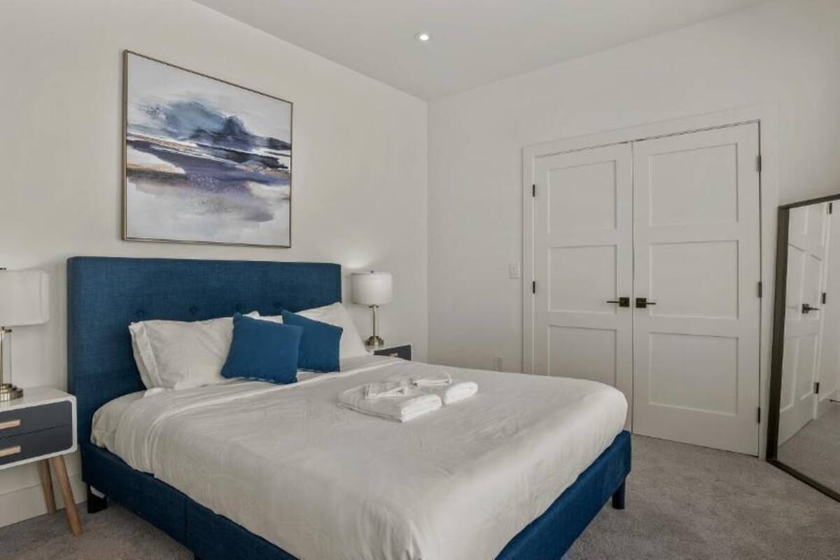 Quarto com cama, mesas de cabeceira, espelho, porta e um quadro na parede.