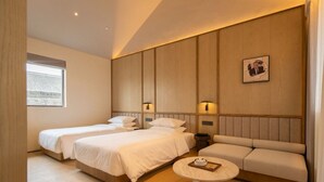 Quarto de hotel com duas camas, um sofá, uma mesa redonda e uma janela.