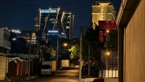 Cena urbana noturna com edifícios, carros estacionados e um letreiro visível do McDonald's.