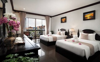 Quarto de hotel com duas camas, uma escrivaninha, um vaso com flores e vista para edifícios.