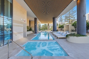 Uma área interna de piscina moderna, com piscina translúcida, espreguiçadeiras e teto com design de ripas exclusivo.