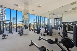 Uma academia moderna com diversos equipamentos de exercício, grandes janelas e vista para a paisagem urbana.