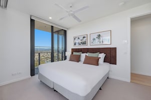 Quarto com uma cama grande, um ventilador de teto e vista para a cidade através de uma janela ampla.