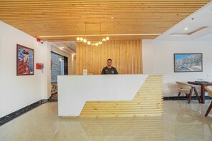 Um balcão de atendimento com design em ripas de madeira, uma pessoa atrás dele e um quadro na parede.