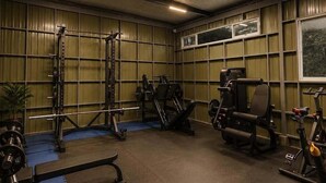 Uma academia com equipamentos de musculação, bicicletas ergométricas e um ventilador de teto.