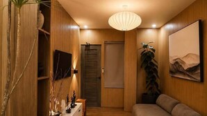 Uma sala de estar moderna com um sofá, uma televisão, paredes de madeira, uma luminária no teto e um quadro.