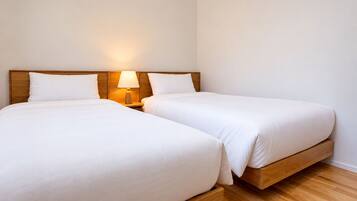 Quarto de hotel com duas camas, mesa de cabeceira com abajur e piso de madeira.
