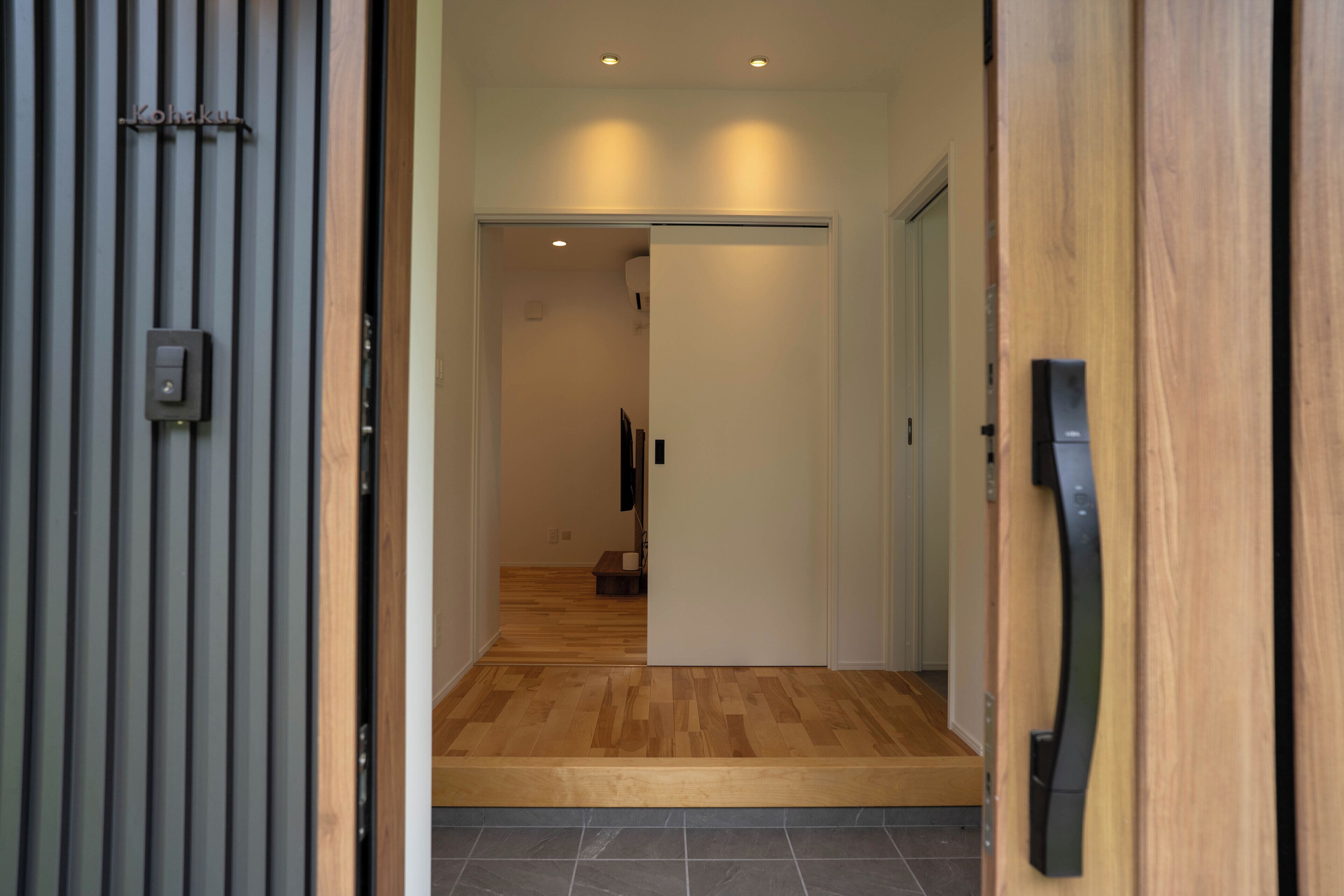 Um interior moderno com piso de madeira, entrada revestida de azulejos e porta com puxador.