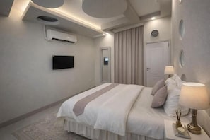 Quarto de hotel moderno com cama, televisão de tela plana, ar condicionado, luminária de cabeceira e uma porta.