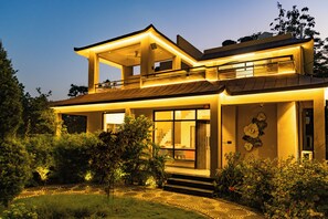 Uma casa moderna de dois andares com varanda, grandes janelas e um jardim bem cuidado.