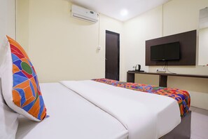 Quarto de hotel com cama, ar condicionado, televisão e escrivaninha com chaleira.