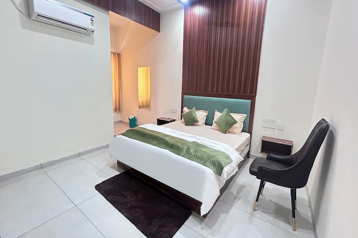 Quarto de hotel com cama, escrivaninha, cadeira e ar condicionado fixado na parede.