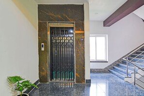 Um corredor com piso de mármore, um portão de metal, um vaso de plantas e uma escada com grades de metal.