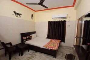 Um quarto com cama, ventilador de teto, ar condicionado, uma mesinha e uma cadeira.