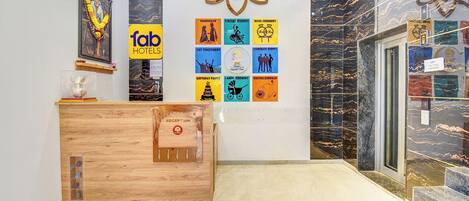 Uma área de recepção de hotel com uma mesa de madeira, placa de recepção e um painel com cartazes de eventos.
