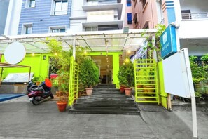 Entrada de um edifício com toldo verde, plantas em vasos e uma motocicleta estacionada na frente.