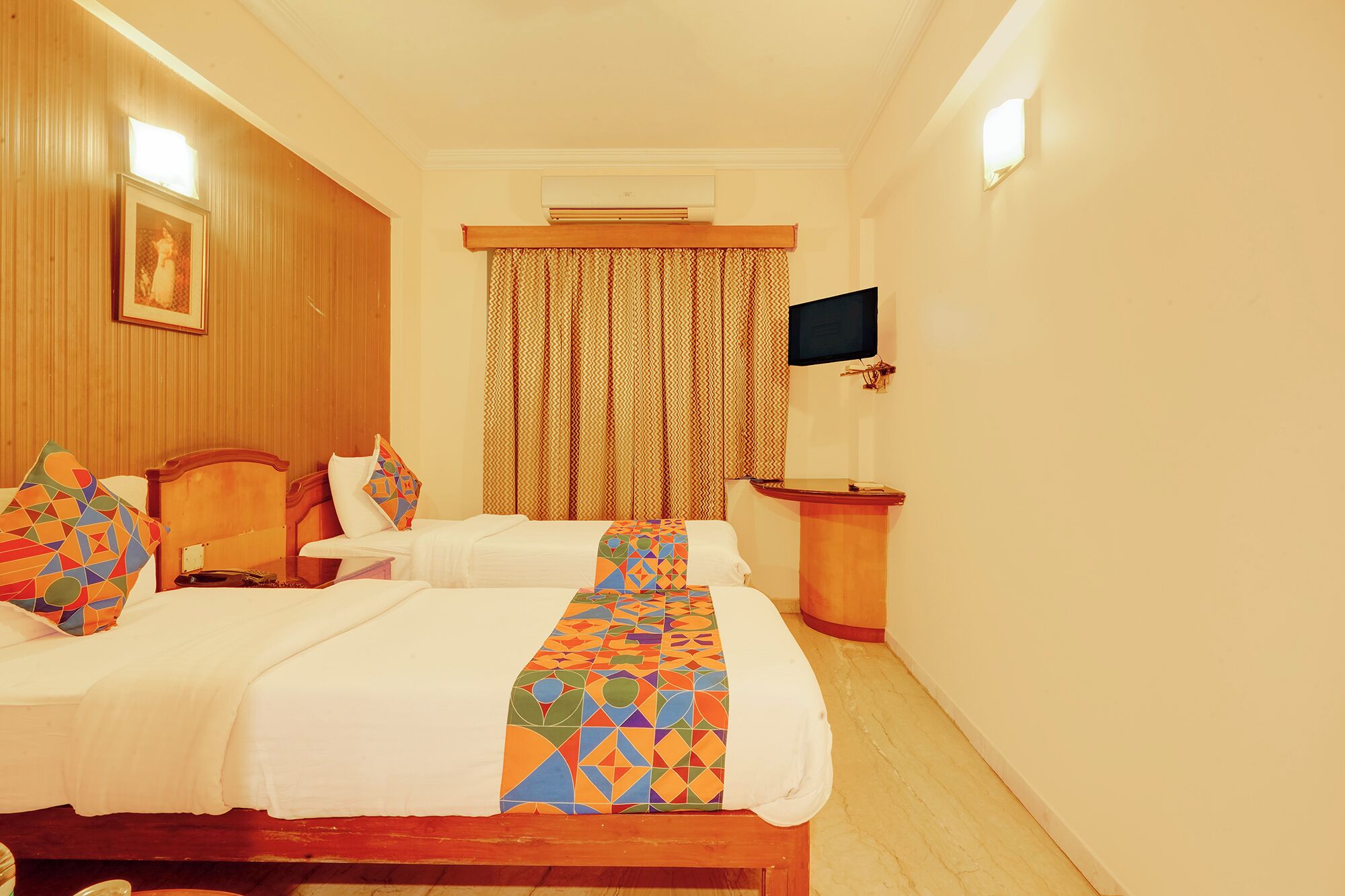 Quarto de hotel com duas camas, televisão, ar condicionado e cortina estampada.