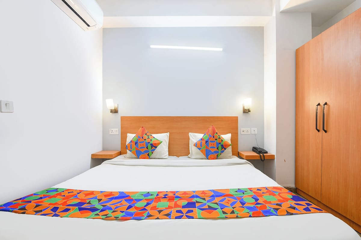 Quarto de hotel com cama, guarda-roupa de madeira, mesa de cabeceira e luminária.