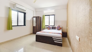 Quarto com cama, guarda-roupa, ventoinha no teto e duas janelas com cortinas.