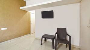 Quarto com piso de azulejos, televisão fixada na parede, um banquinho e uma cadeira.