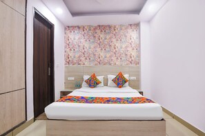Quarto de hotel com cama, duas almofadas, mesa de cabeceira e parede com padrão abstrato colorido.