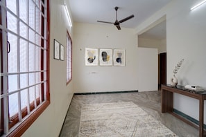 Um corredor com ventoinha no teto, obras de arte emolduradas na parede, um aparador com um vaso e livros, e um tapete estampado no chão.