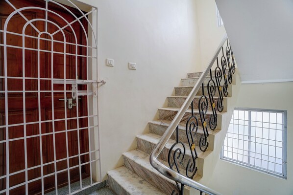 Uma escadaria com guarda-corpo de metal, uma porta de madeira com grade metálica e uma janela com grade de metal.