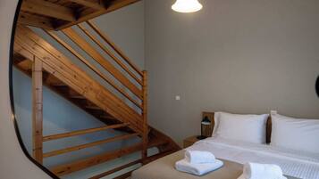 Quarto com escada de madeira, cama com roupa de cama branca e luminária de cabeceira.