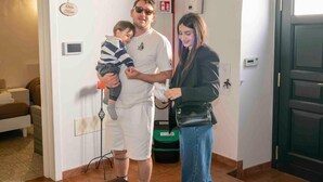 Uma família com uma criança em um corredor, com uma lixeira verde, um alarme de incêndio e uma porta.
