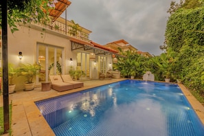 Piscina com espreguiçadeiras, varanda coberta e plantas em vasos.
