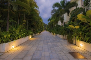 Um caminho pavimentado ladeado por vegetação exuberante e iluminado por luzes nas paredes.