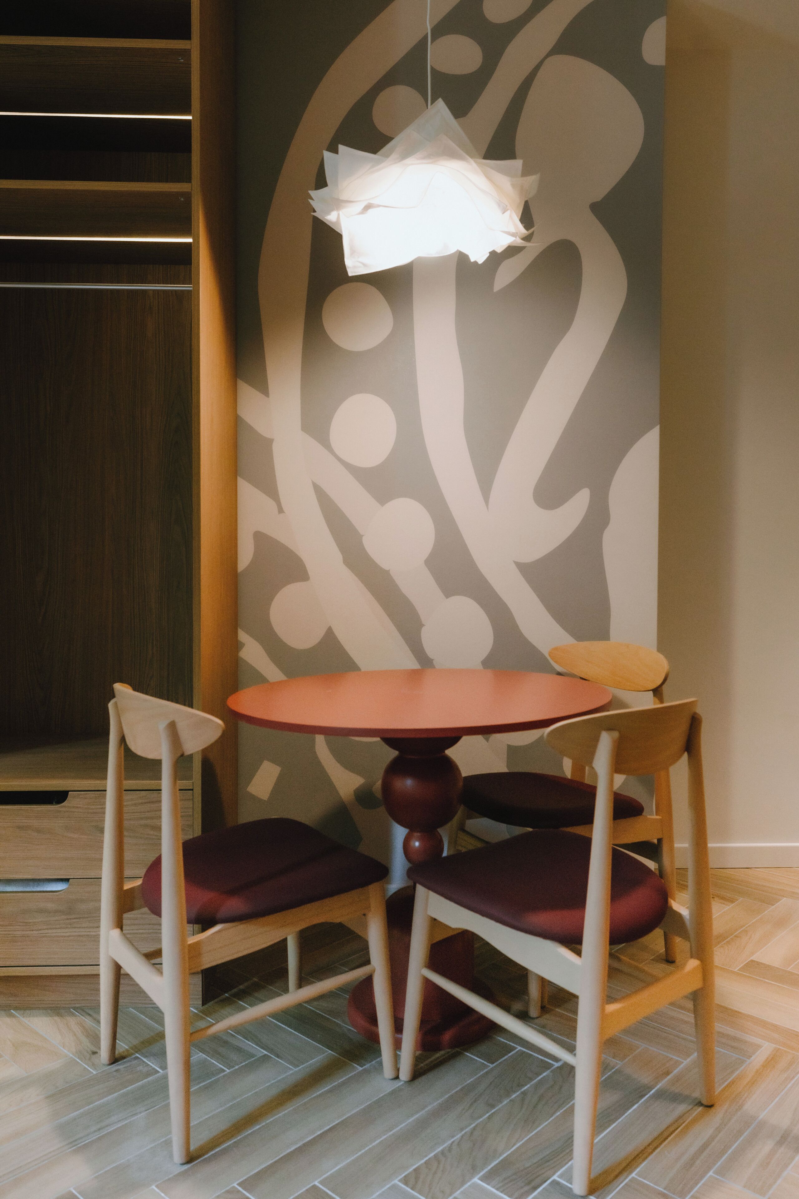 Uma sala de jantar com uma mesa redonda e duas cadeiras, um lustre e um papel de parede estampado.