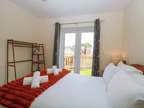 Quarto de hotel com cama, escada de madeira, janela com cortinas e vista para uma cerca e casas lá fora.