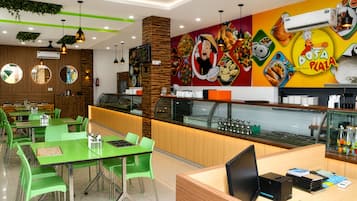 Um restaurante com mesas e cadeiras verdes, um balcão com um computador e uma parede com ilustrações de comida.