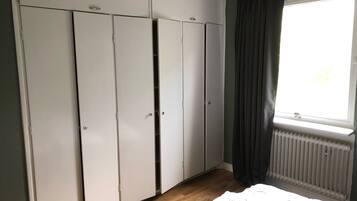 Quarto com um guarda-roupa espaçoso, radiador e janela com cortinas.