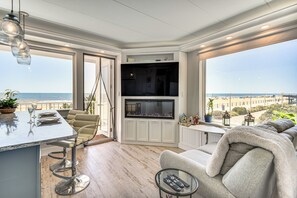 Uma sala de estar moderna com uma televisão grande, assentos confortáveis, uma mesa de vidro e vista para a praia.