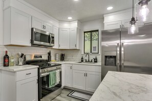 Uma cozinha moderna com armários brancos, eletrodomésticos de aço inoxidável e bancada de mármore.
