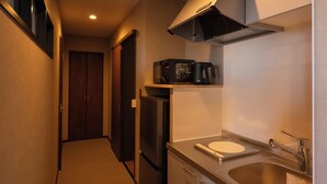 Um corredor estreito que dá para uma cozinha compacta, com geladeira, micro-ondas e pia.
