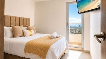 Quarto de hotel com cama, televisão na parede e vista para a cidade pela janela.