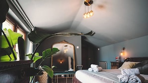 Quarto com uma cama grande, um espelho, uma planta e um lustre.