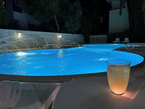Piscina com elementos aquáticos, cadeiras de descanso e um copo de bebida sobre uma mesa.