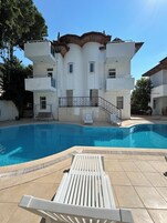 Um edifício de dois andares com piscina, área de estar externa e escadaria que leva ao andar superior.