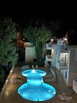 Uma piscina com design em níveis, rodeada por espreguiçadeiras e um edifício com varandas.