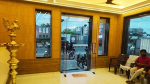 Uma área de recepção com interior em madeira, uma luminária dourada decorativa e vista para a rua.