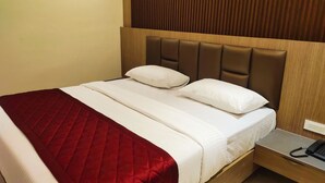 Quarto de hotel com uma cama, mesa de cabeceira e cabeceira de madeira.