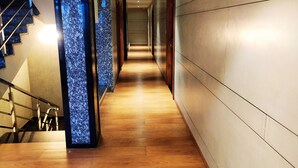 Corredor moderno de hotel com piso de madeira, um pilar de mármore e uma escadaria.