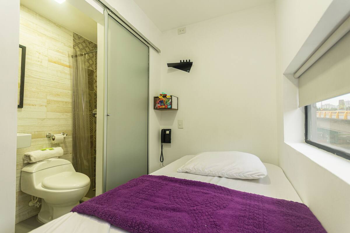 Um quarto pequeno e moderno com uma cama, chuveiro, vaso sanitário e janela.