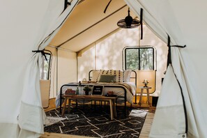 Um quarto com tenda, uma cama, uma mesinha com um aviso, um abajur e uma janela.